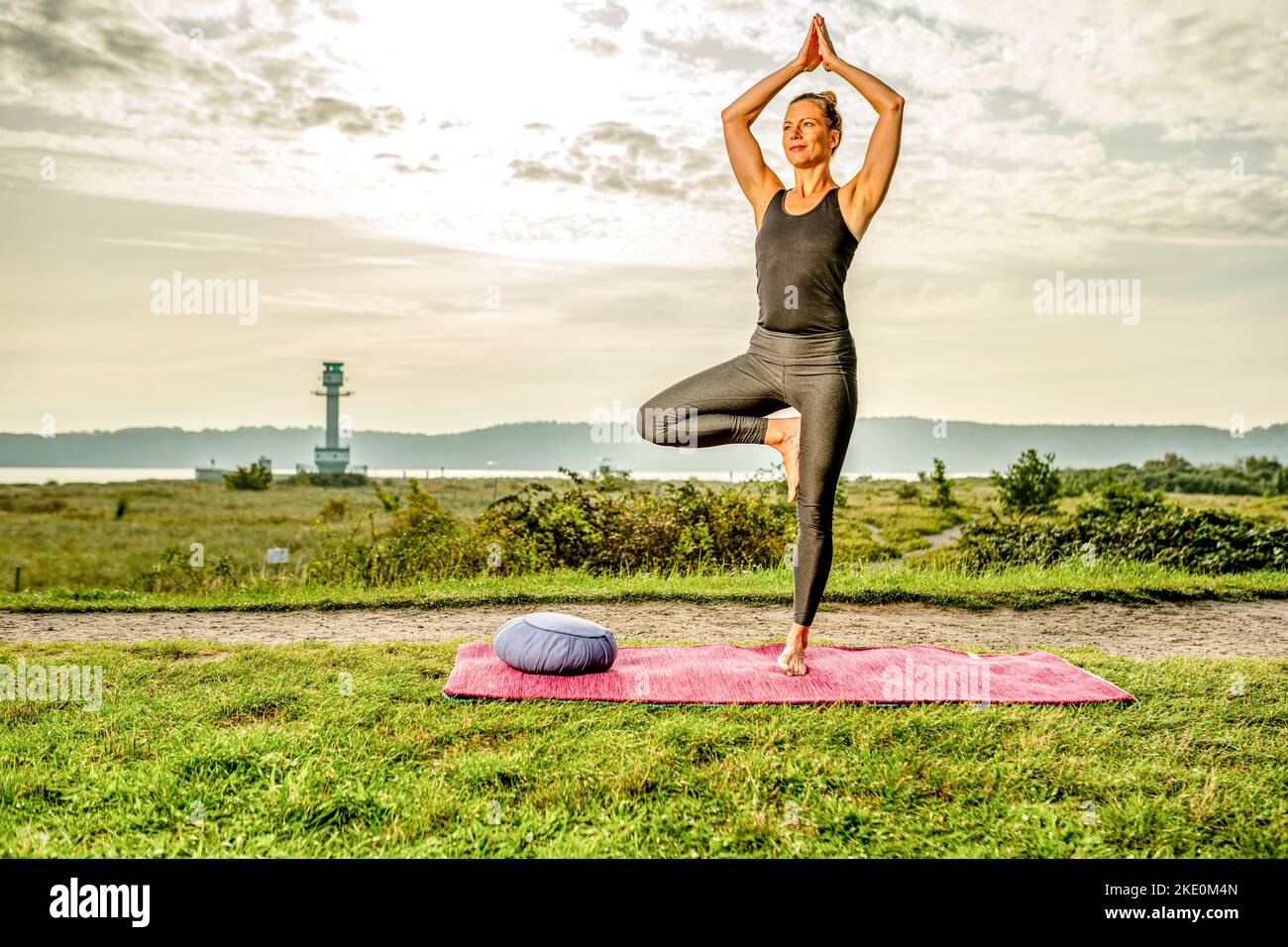 A caucasian woman practicing yoga in a tree pose in nature at sunrise ...