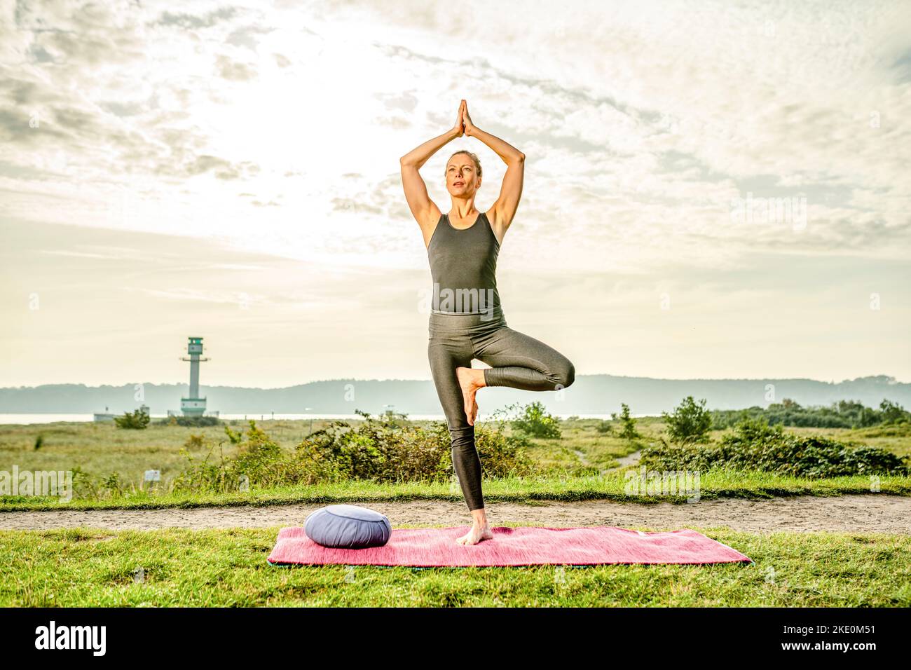 A caucasian woman practicing yoga in a tree pose in nature at sunrise ...