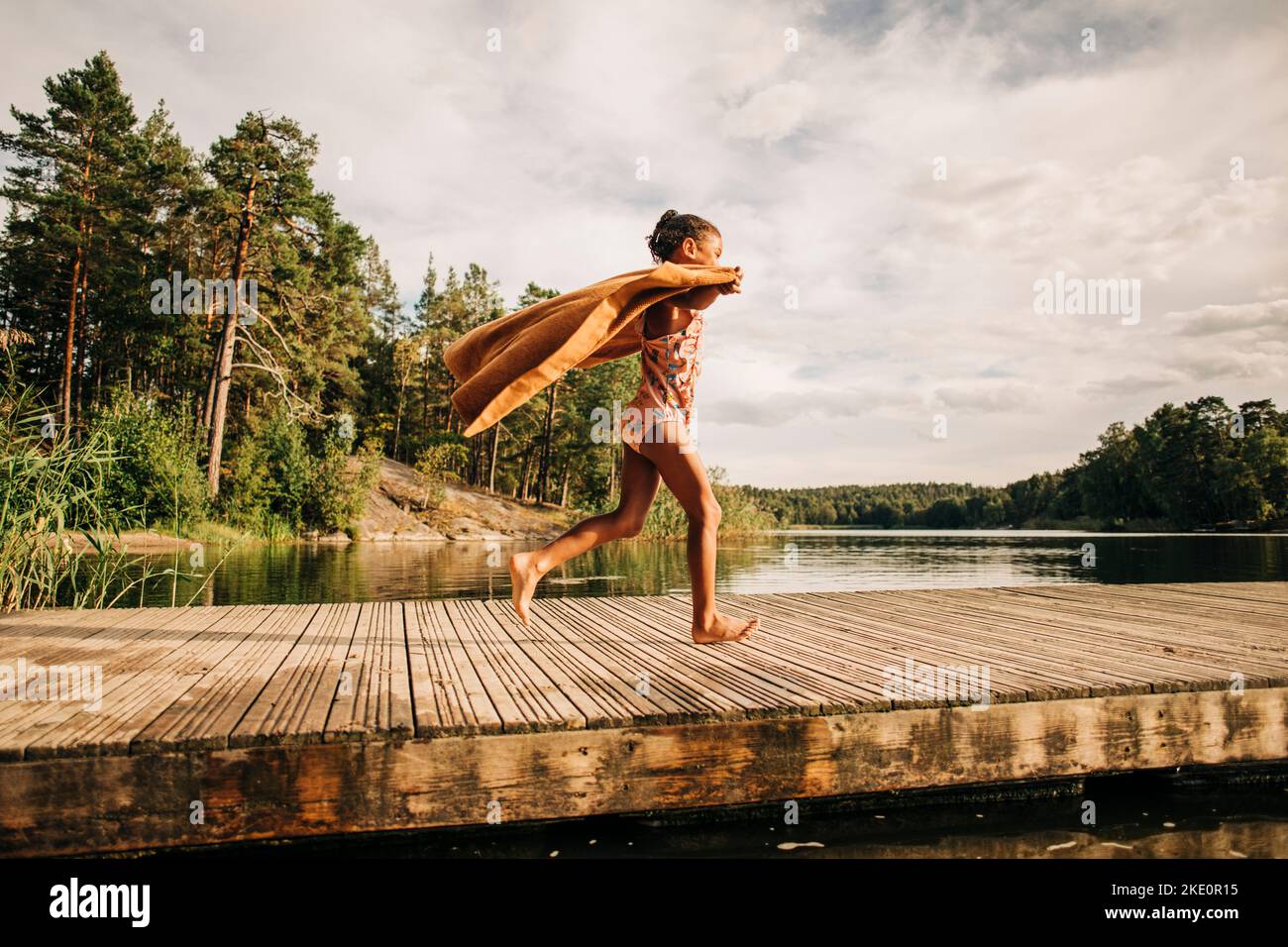 Side view of girl running on jetty while holding towel Stock Photo - Alamy