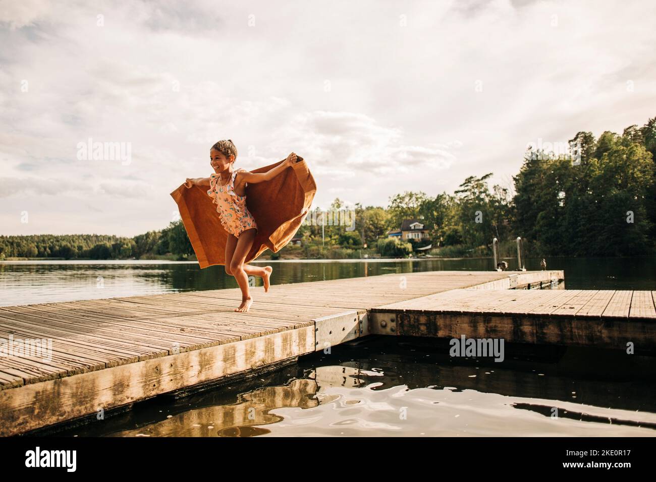 Carefree girl running on jetty while holding towel during vacation ...