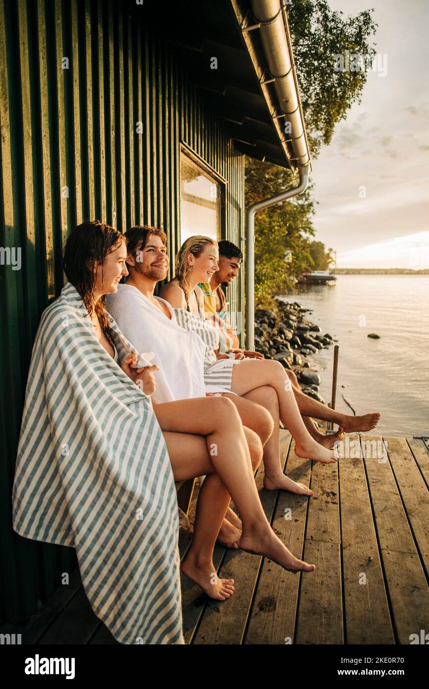 Male and female friends sitting near cottage with legs crossed at knee ...
