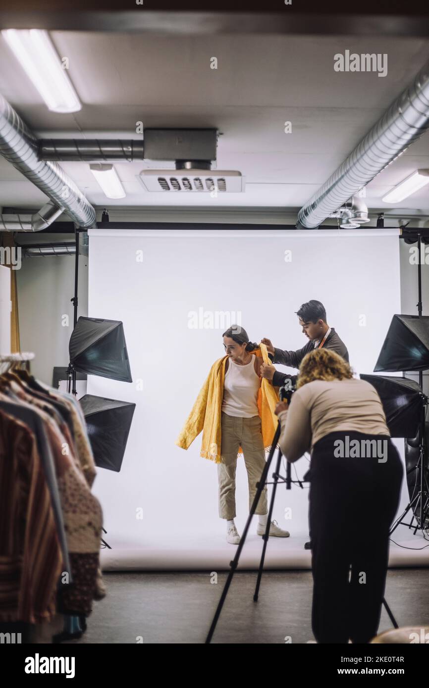Photographer photographing designer helping model wearing jacket ...