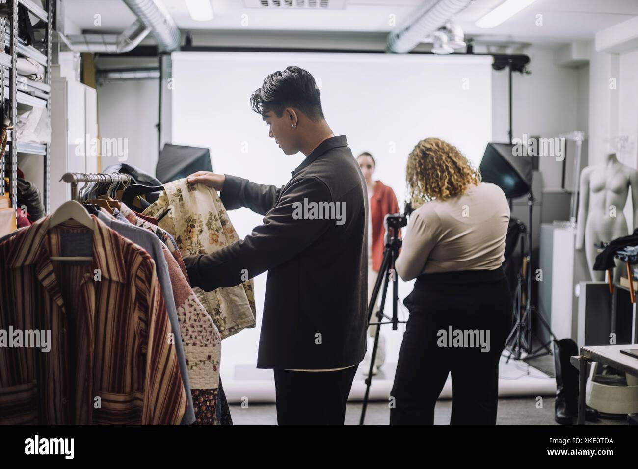 Side view of male designer choosing clothes from rack during photo ...