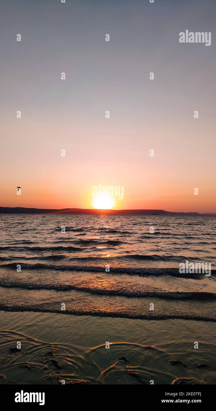 The bright sun shining in orange and blue sunset sky over the water ...