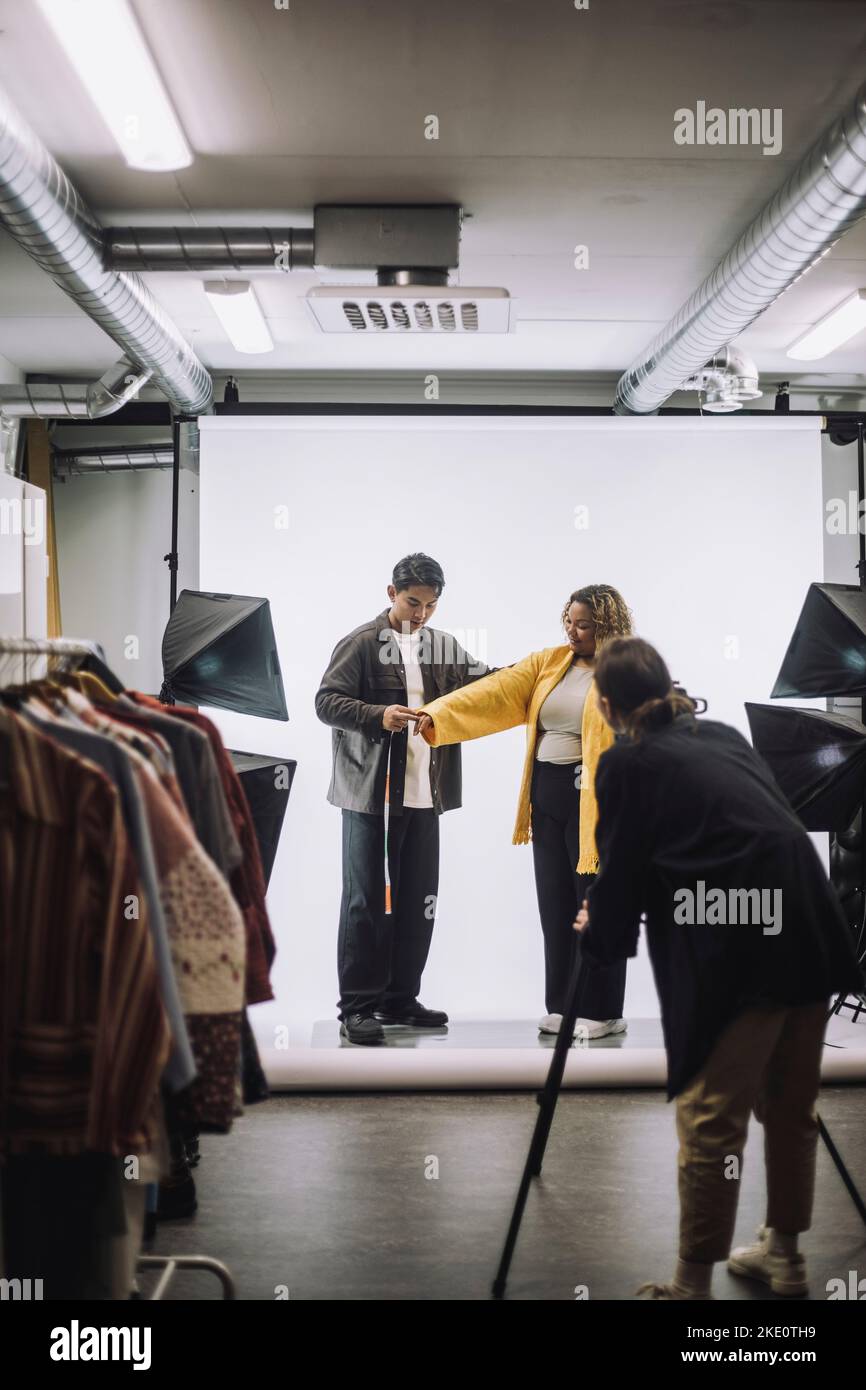 Male fashion designer taking measurement of model during photo shoot at ...