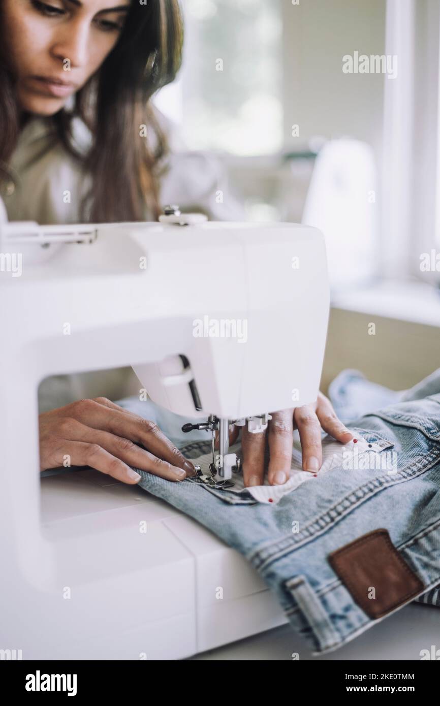 Female fashion designer sewing fabric on jeans pocket using sewing ...