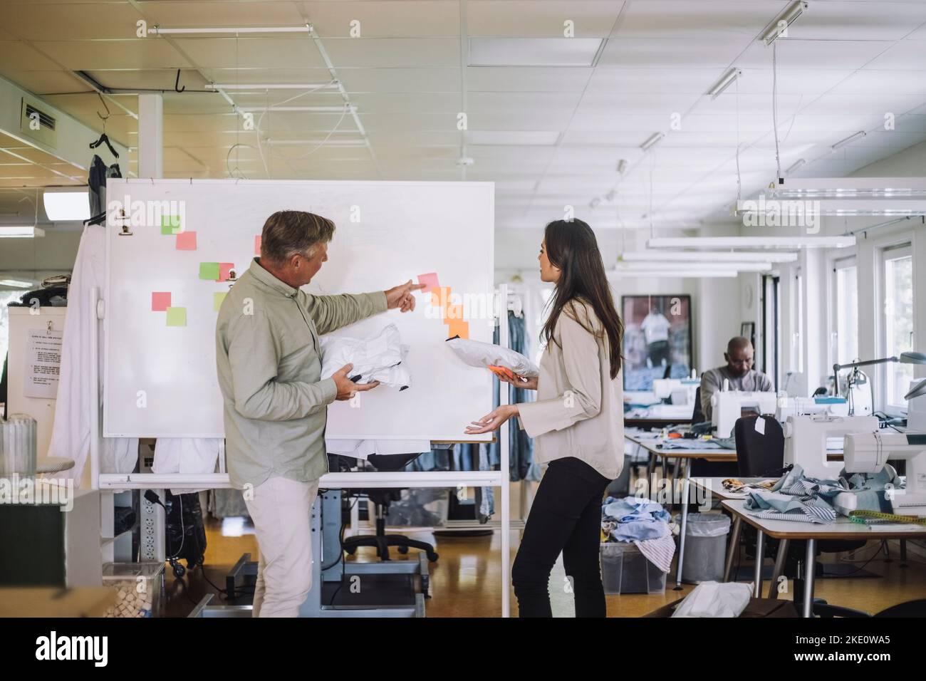Side view of male fashion designer explaining female colleague on ...