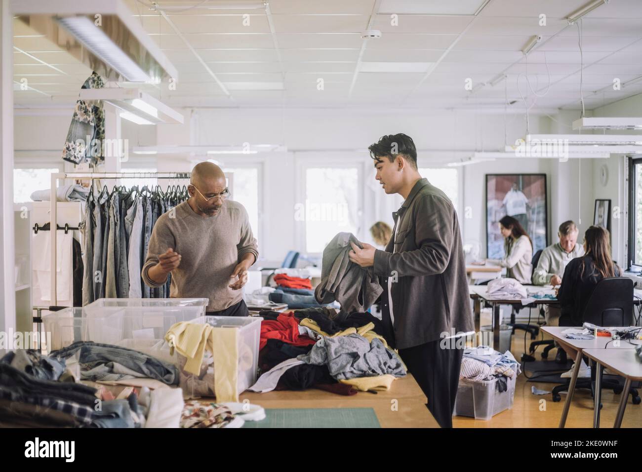 Male fashion designers discussing with each other while sorting ...