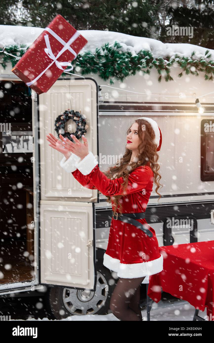 Beauty girl in santa costume with gift box at winter campsite getting ready for the new year ...