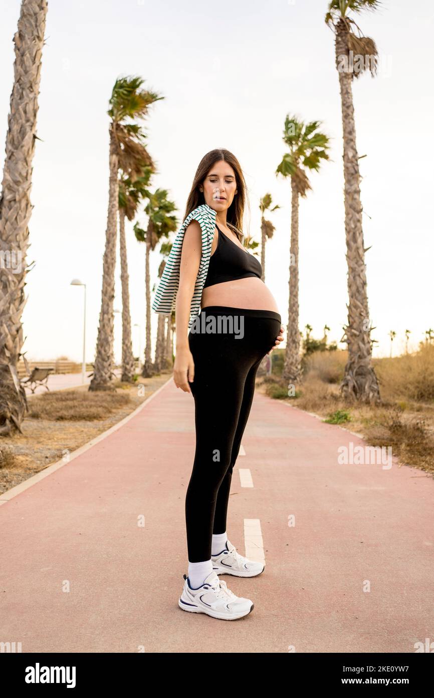 pregnant young woman with long brown hair wears sportswear and does ...