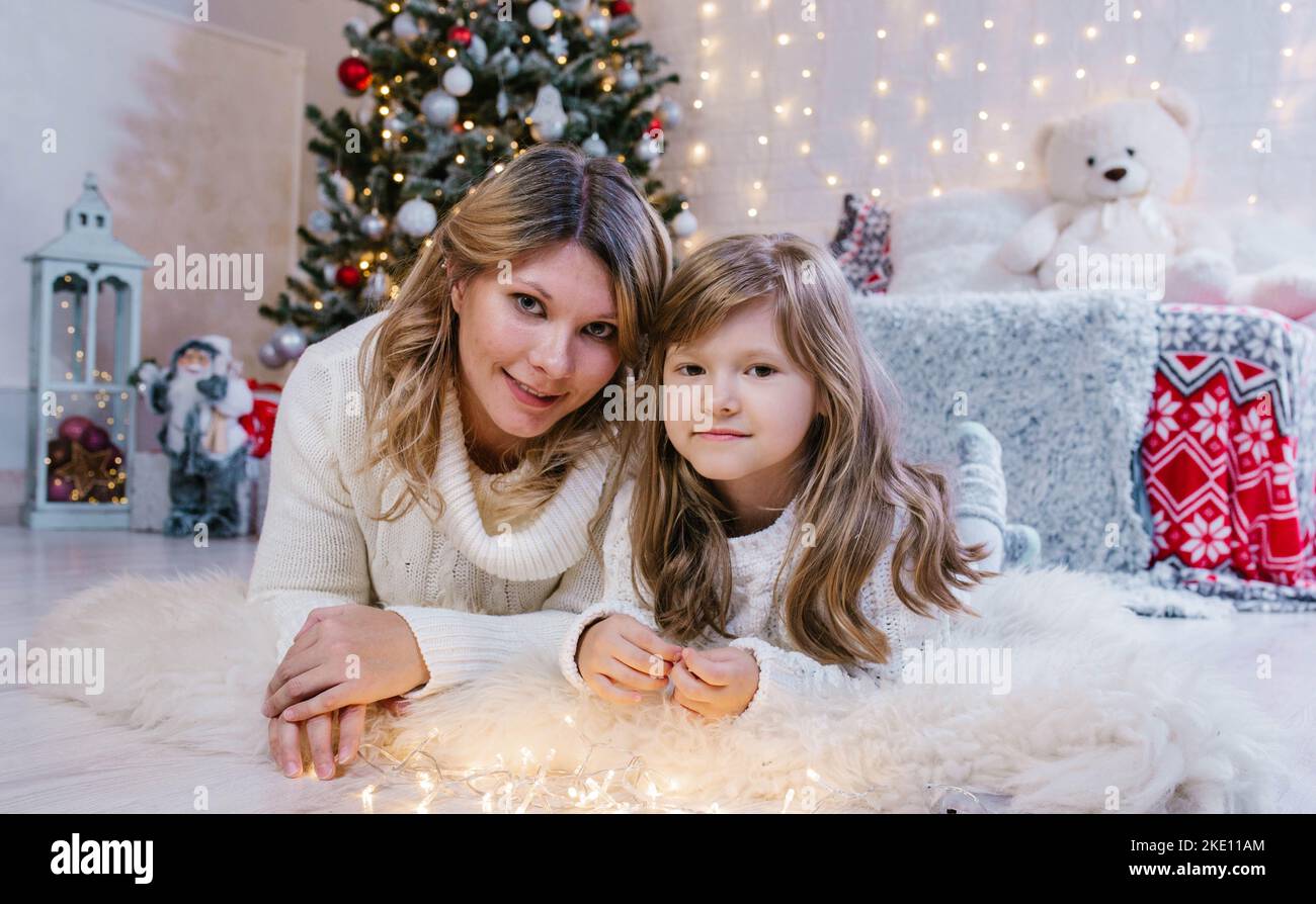 Mother and daughter in white sweaters lie on the white carpet on the ...