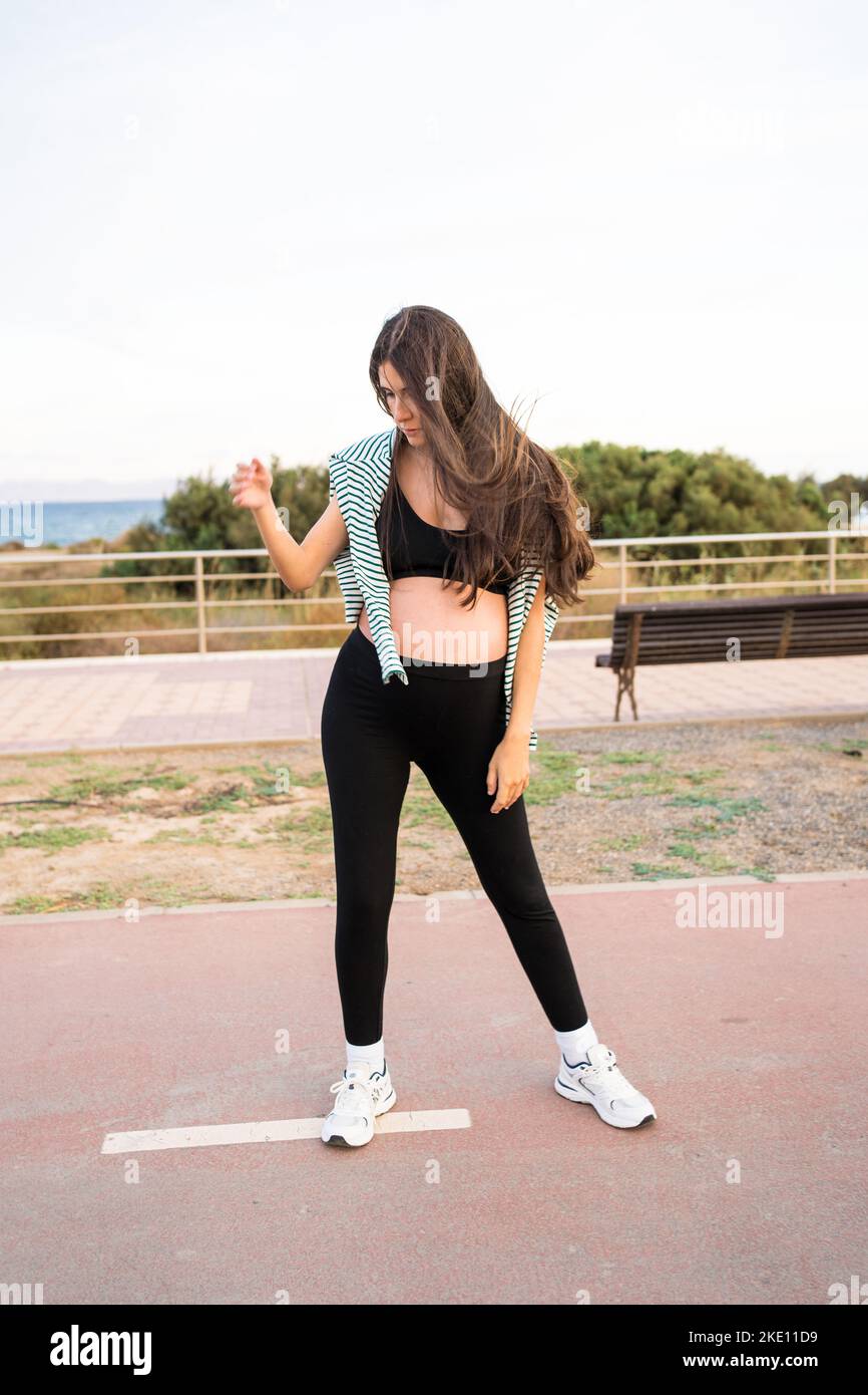 pregnant young woman with long brown hair wears sportswear and does ...