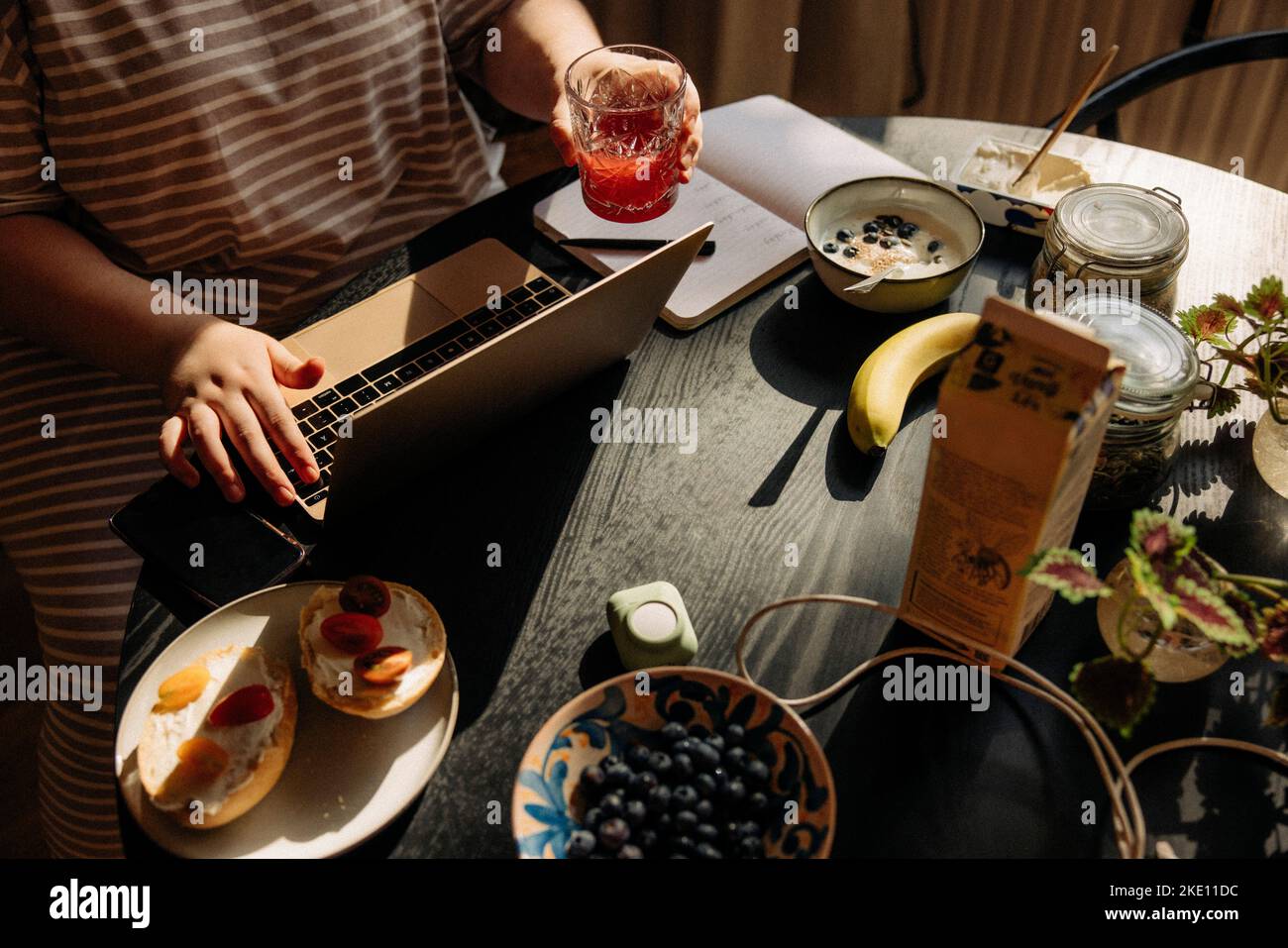 High angle view of woman holding drinking glass while using laptop with ...