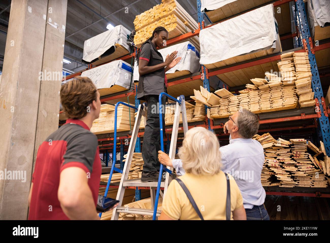 Saleswoman standing on ladder gesturing while talking with customers at ...