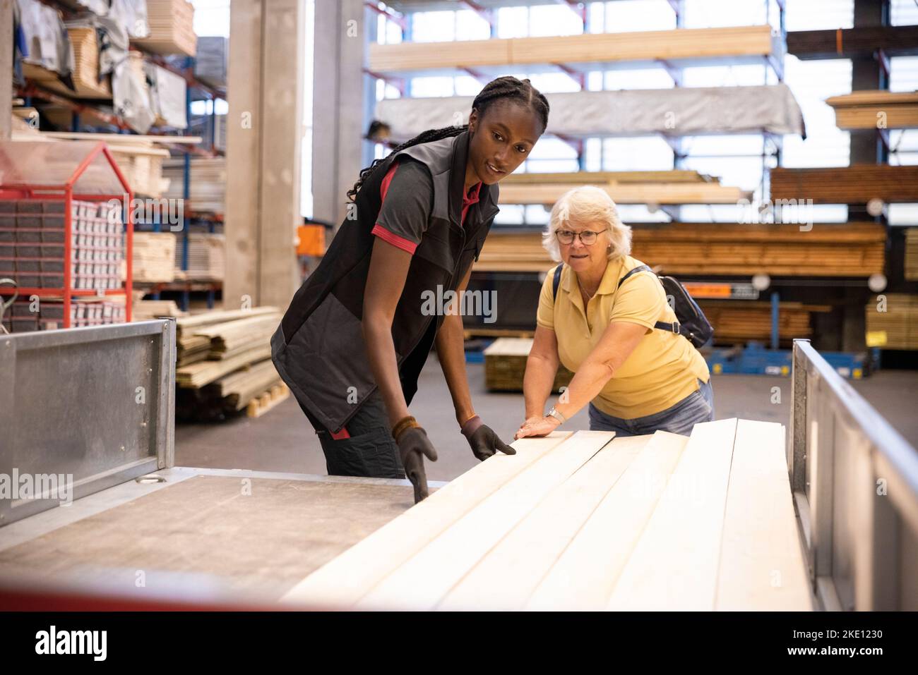 Saleswoman helping senior woman while loading plank in trailer at ...