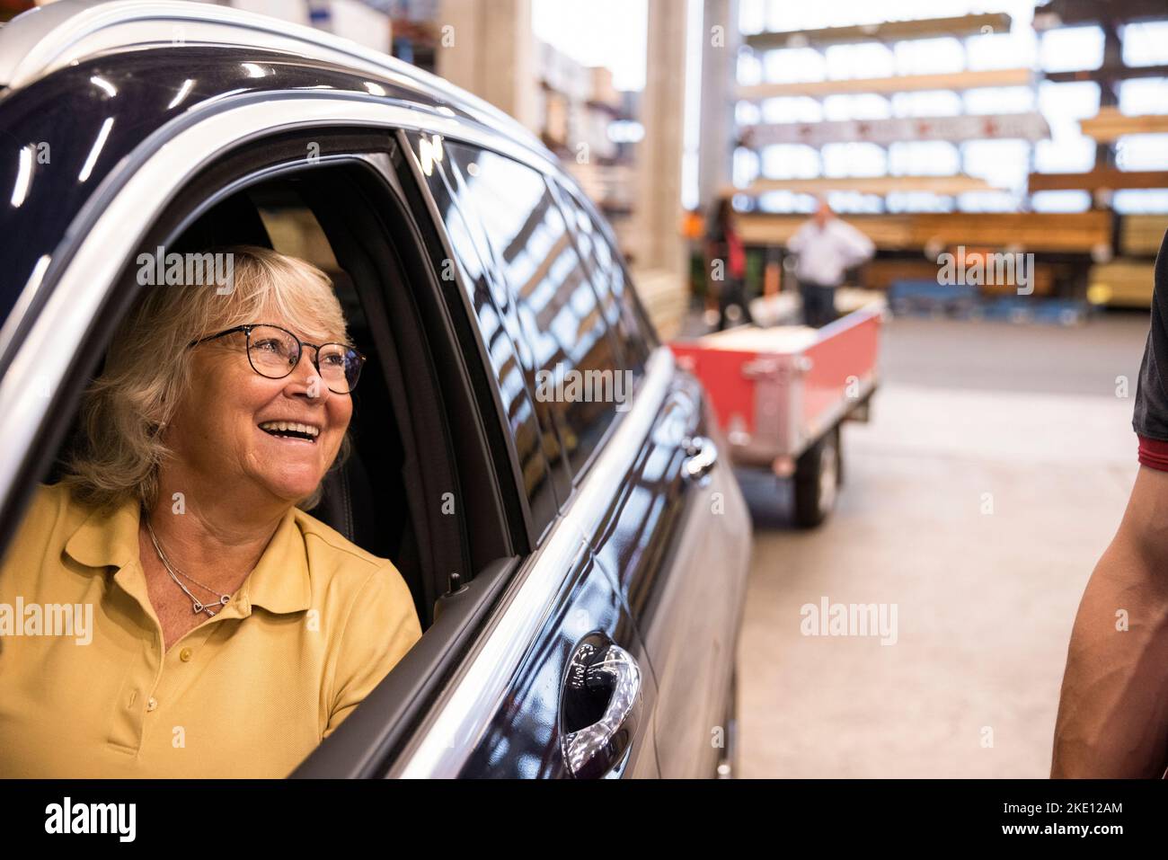 Happy female customer sitting in car looking at sales staff in hardware ...