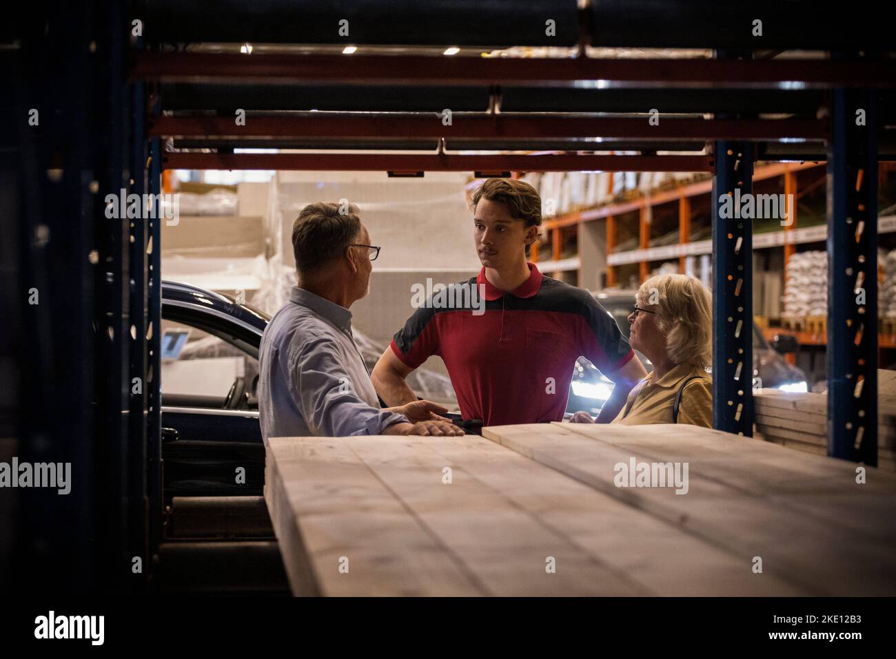 Senior male and female customer talking to salesman seen through rack ...