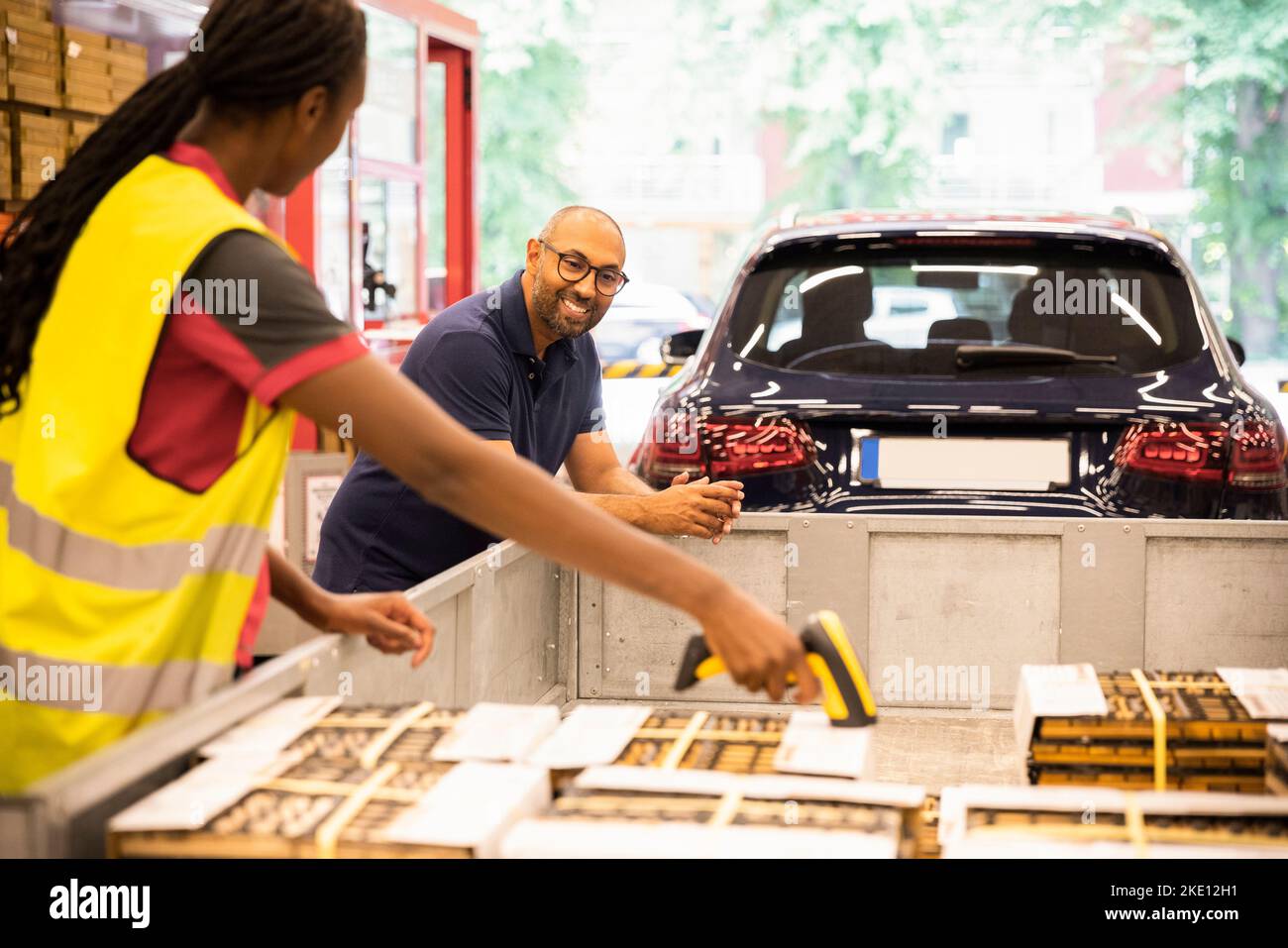 Smiling male customer leaning on trailer while talking to sales staff ...