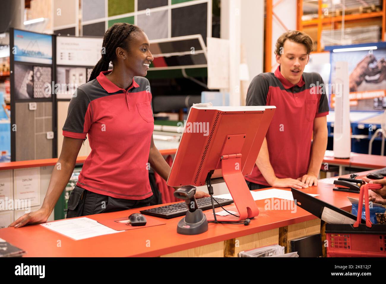 Smiling female cashier with male colleague standing at checkout in ...