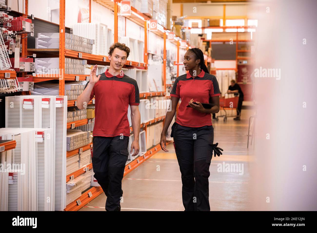 Male and female sales staff talking while walking in hardware store ...