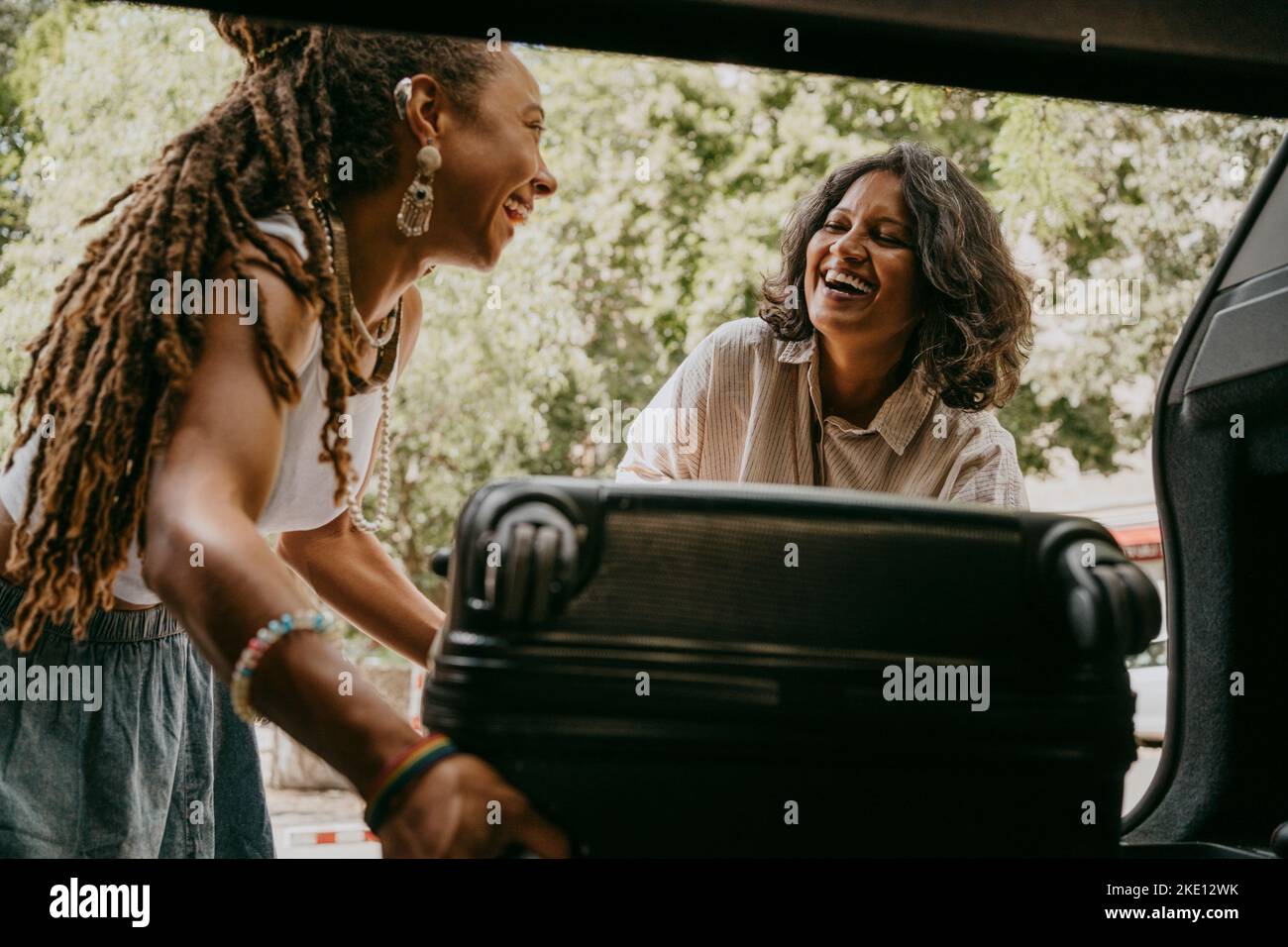 Happy female partners unloading suitcase from car trunk Stock Photo - Alamy