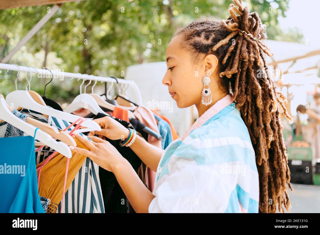 Side view of female customer with dreadlocks buying dress at flea ...