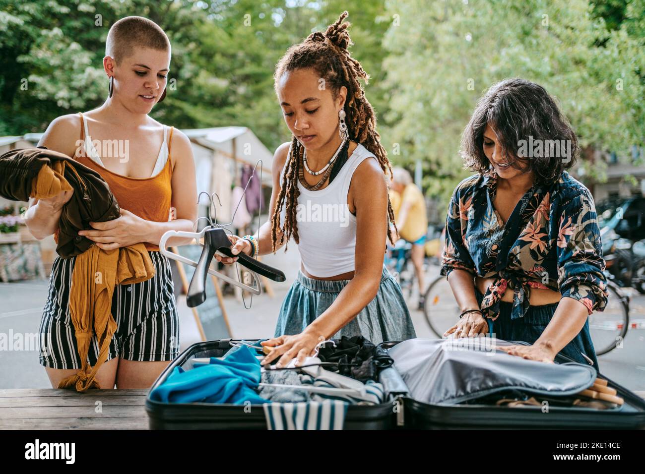 Female partners packing dress in suitcase on table at flea market Stock ...