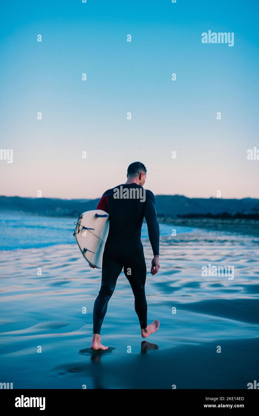 Middle aged surfer walks along the beach Stock Photo - Alamy