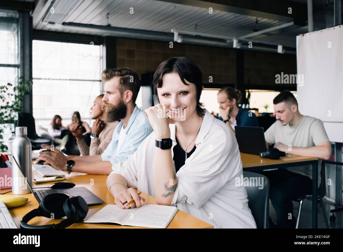 Portrait of smiling non-binary business person sitting by male ...