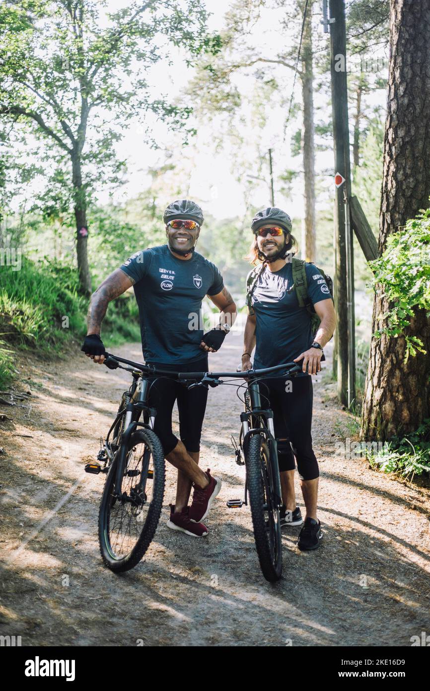 Smiling male friends with cycles standing on footpath Stock Photo - Alamy