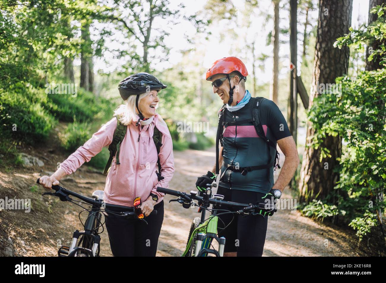 Happy male and female friends talking to each other holding cycles ...
