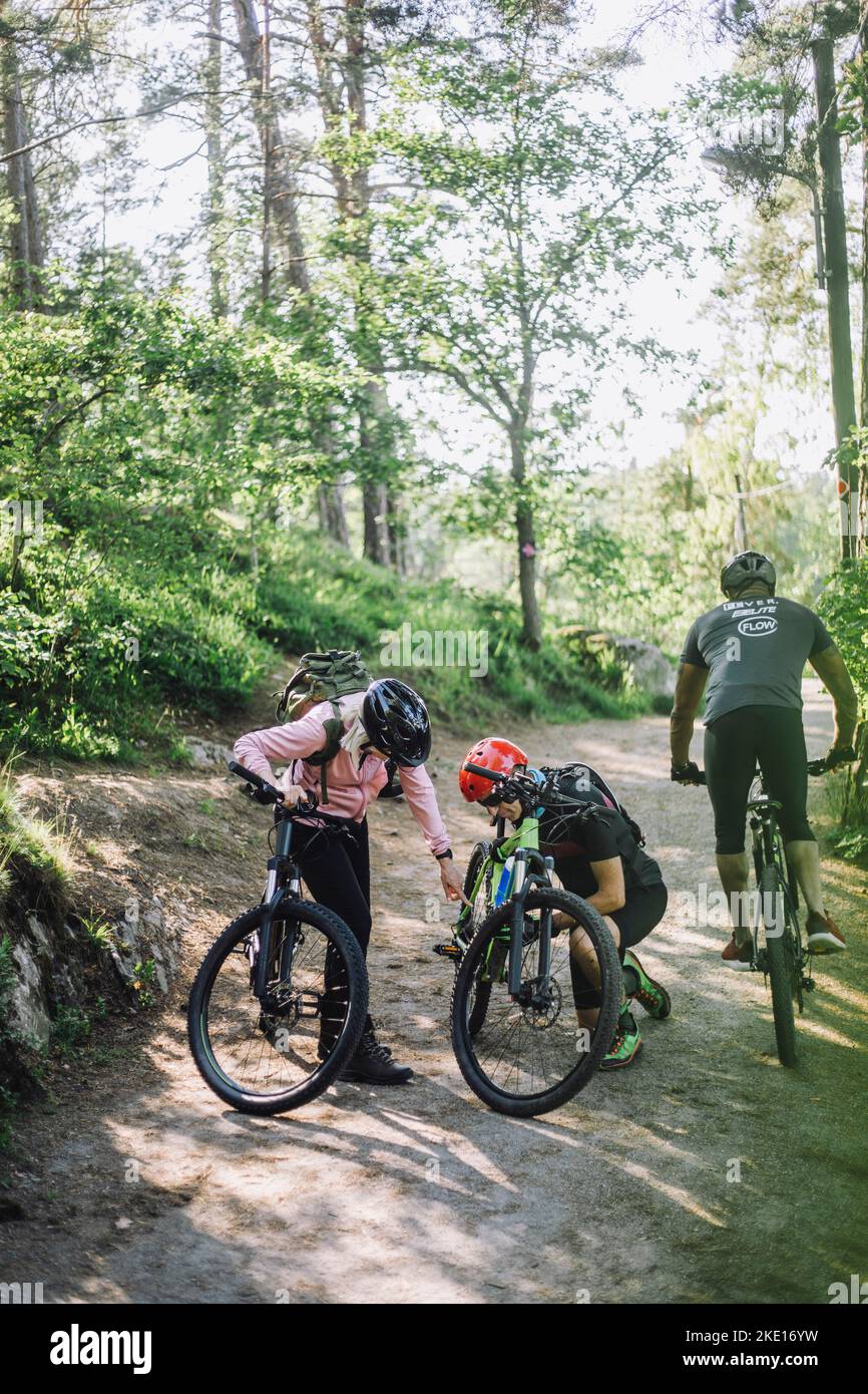 Woman assisting male friend repairing cycle while kneeling on footpath ...