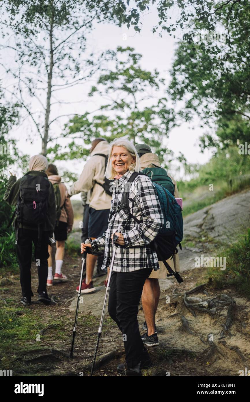 Side view of smiling senior woman holding pole during hiking with ...