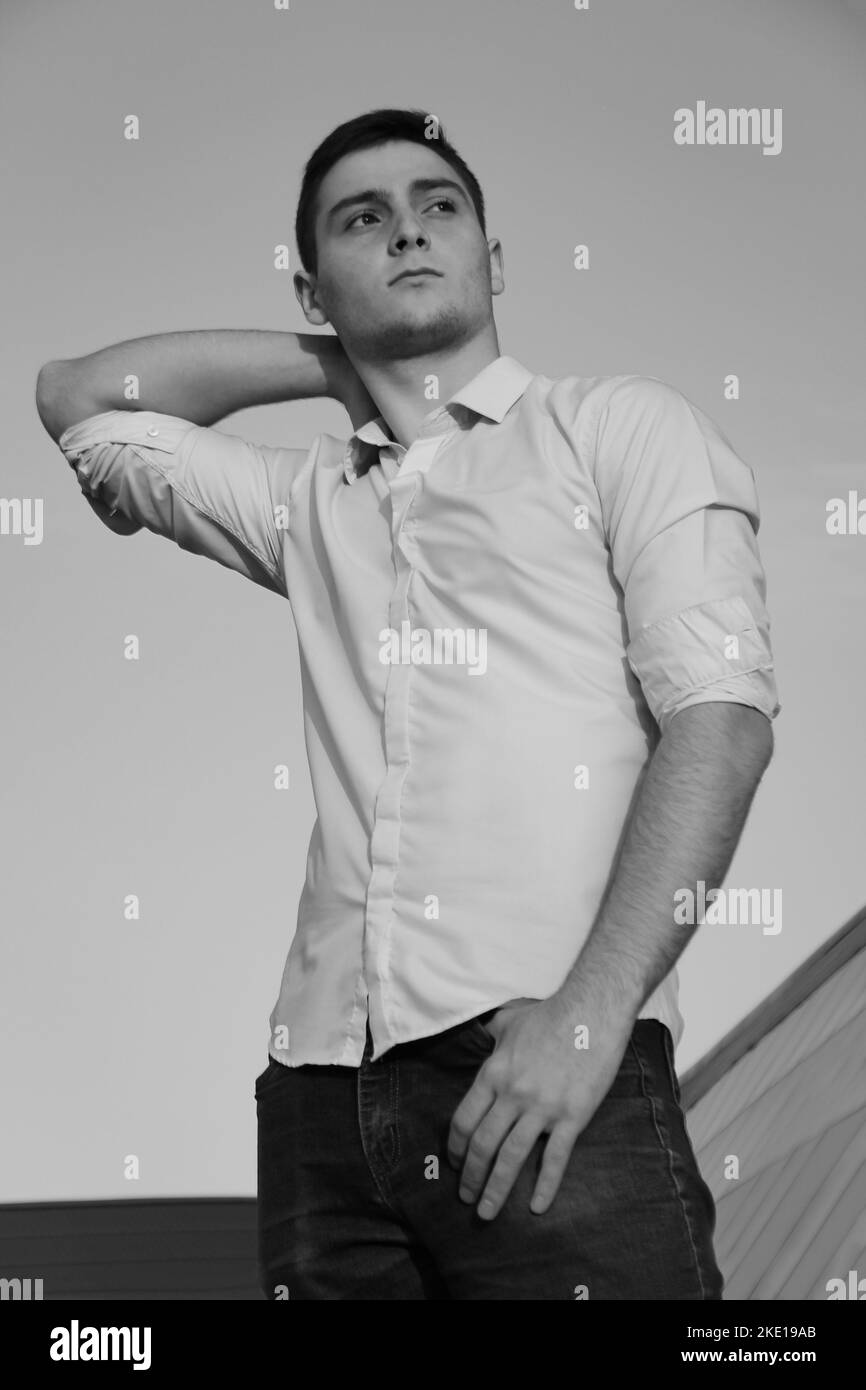 A grayscale of a handsome male in a casual outfit looking side ...