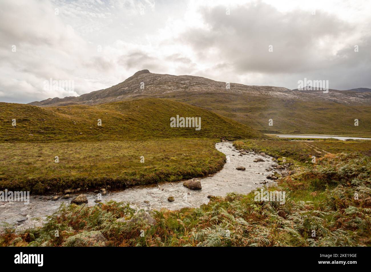 A small water stream surrounded by a meadow and mountains on a gloomy ...