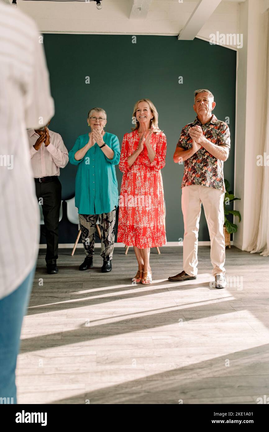 Smiling senior men and women clapping while standing in dance class ...