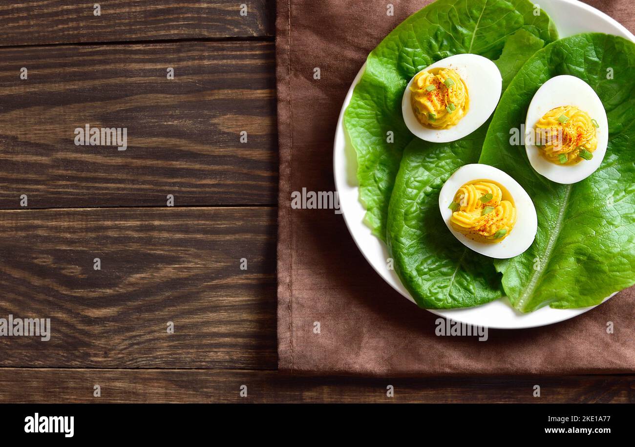 Deviled eggs with paprika, mustard and mayonnaise on plate over wooden ...