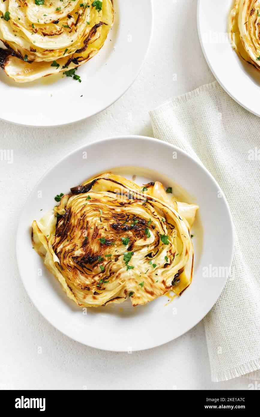 Roasted cabbage steaks on plate over white background. Top view, flat ...