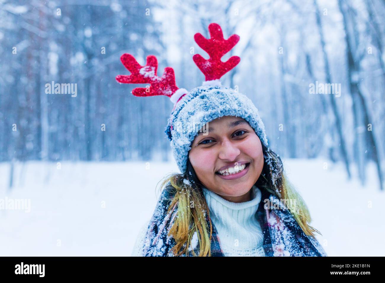 Happy indian woman having fun and enjoying first snow wear fun hat deer ...