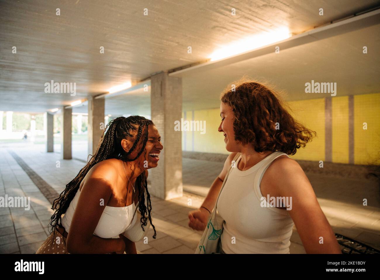 Teenage girl laughing by female friend while enjoying under bridge ...