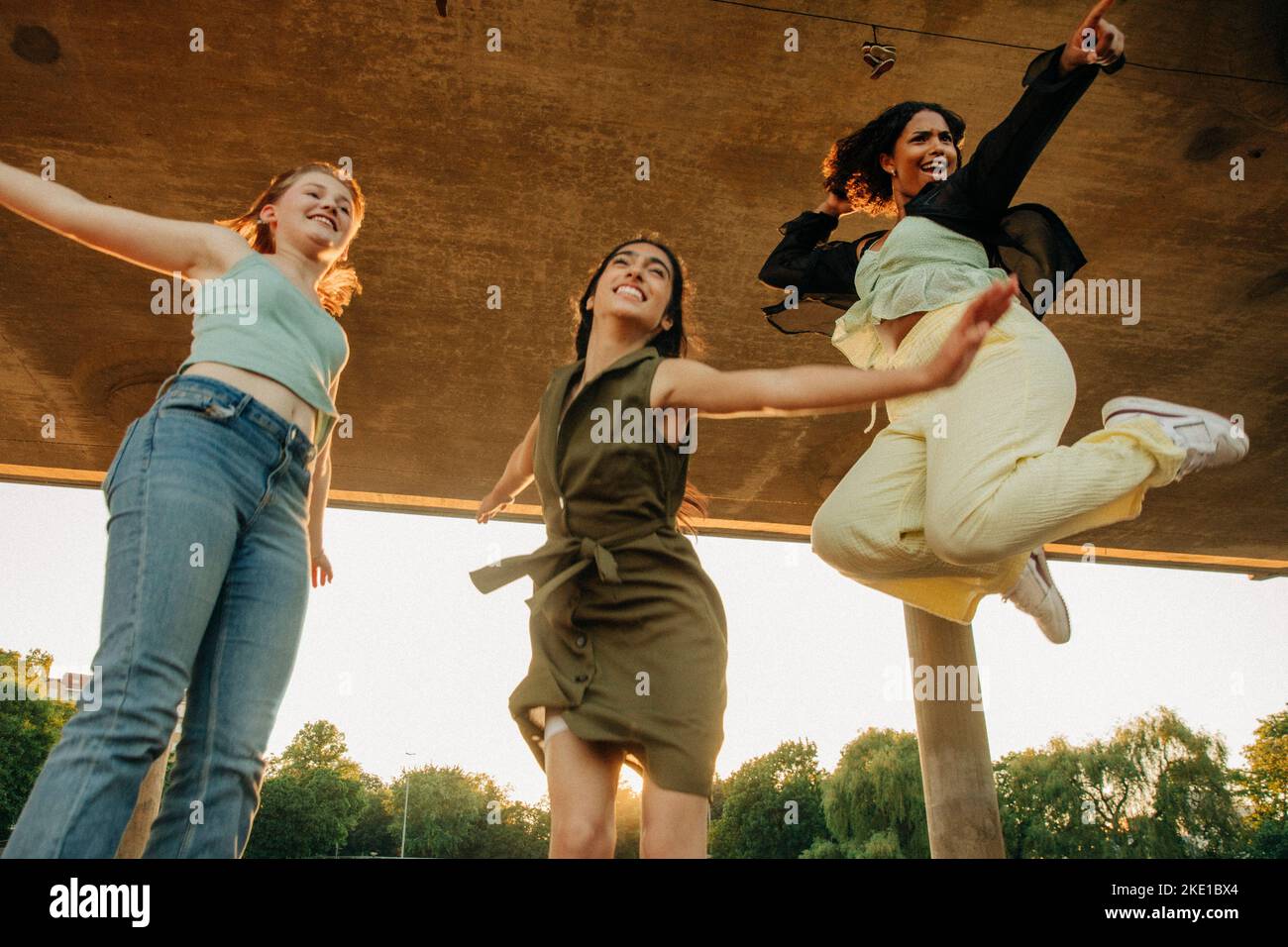 Low angle view of happy teenage girls jumping under bridge Stock Photo ...