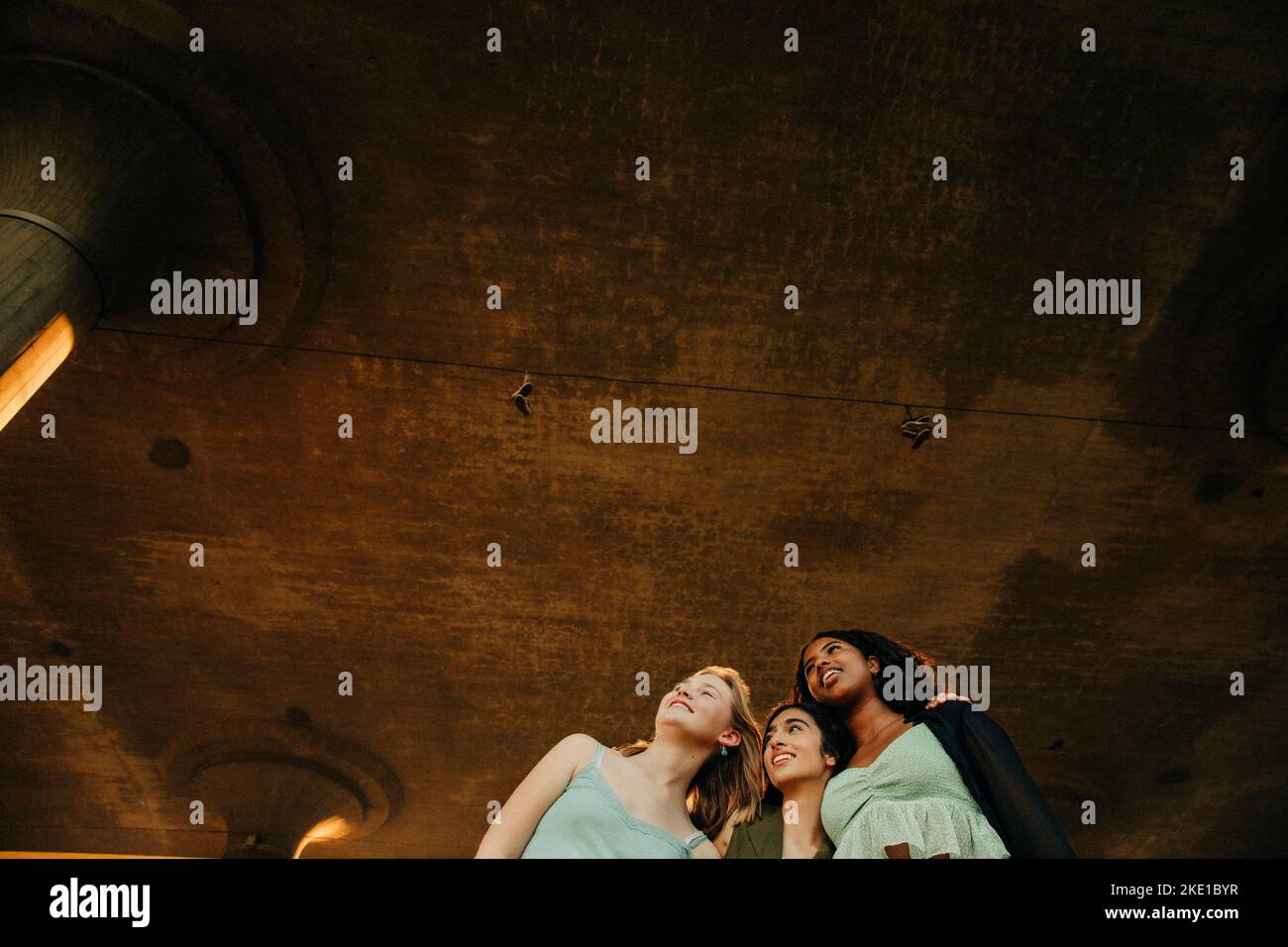 Smiling teenage girls looking away while standing under bridge Stock ...