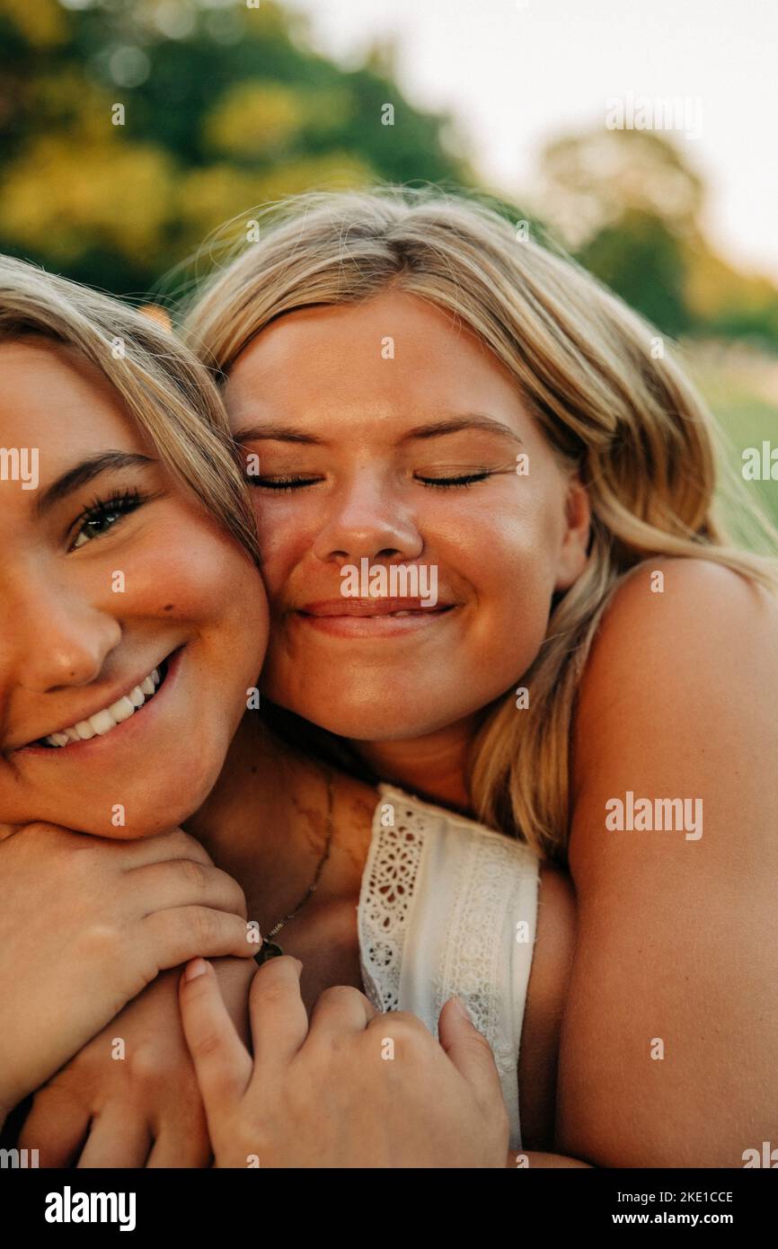 Smiling girl with eyes closed hugging blond female friend Stock Photo ...