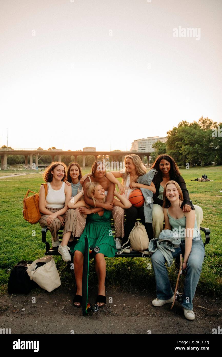 Portrait of happy teenage girls sitting on bench at park Stock Photo ...