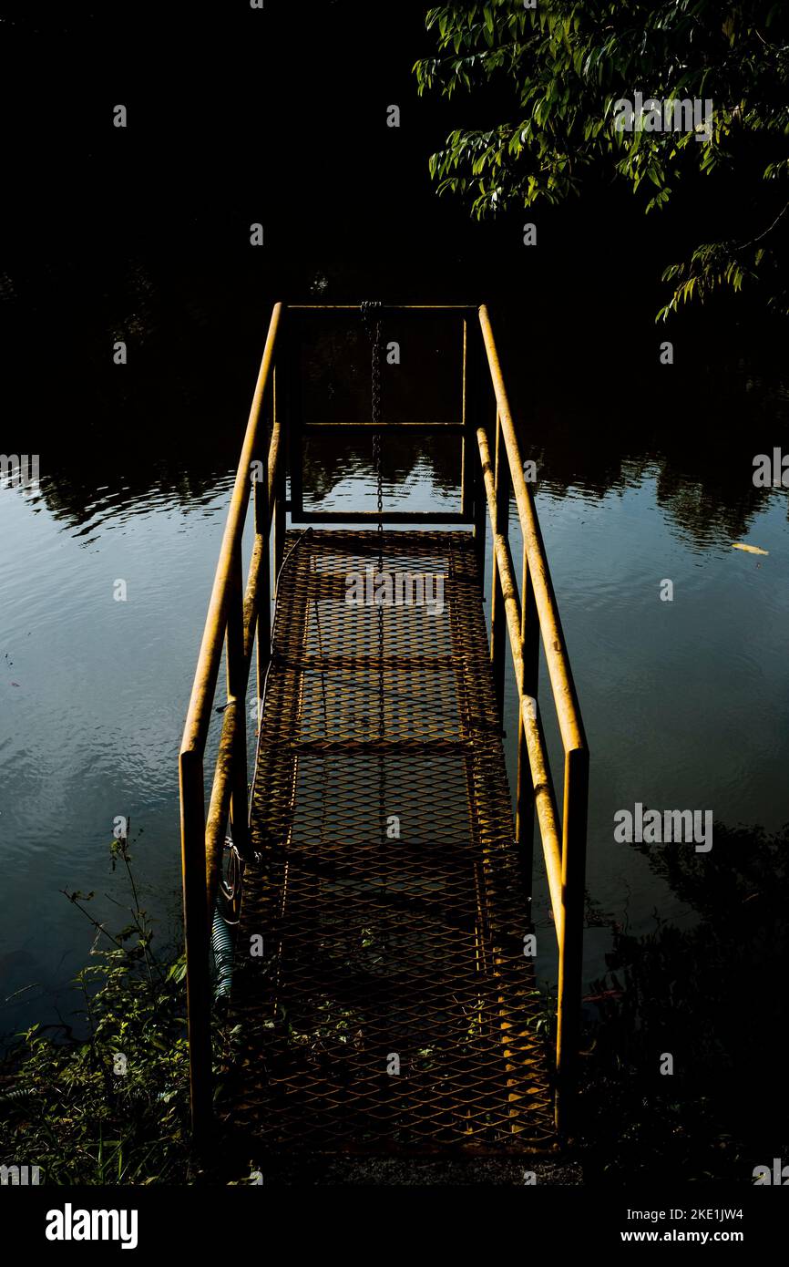 A small yellow metal bridge over river water with green trees with ...