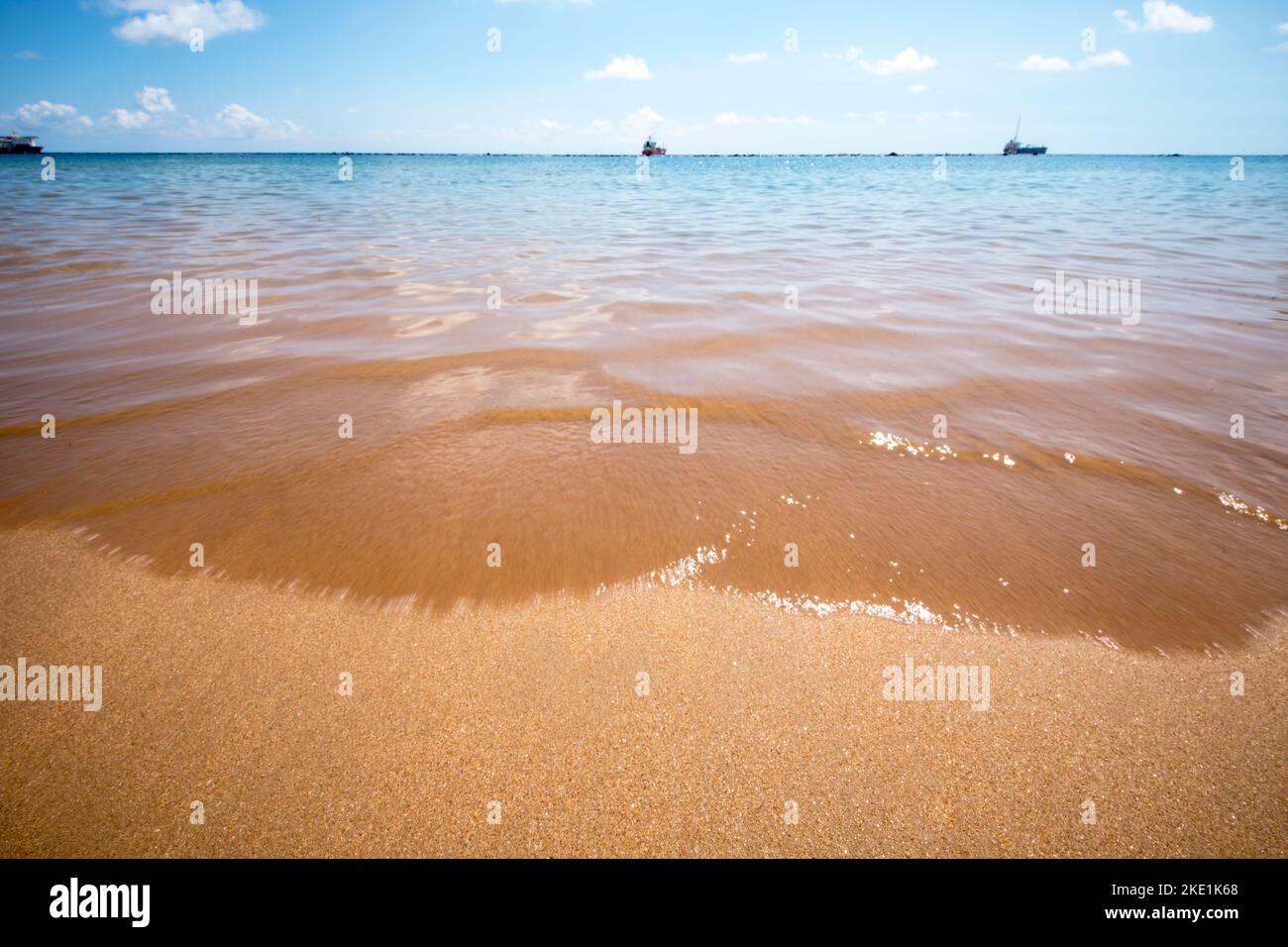 The ocean water crashing the shore with yellow sand and ships floating ...