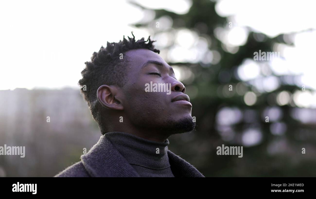 African man taking a deep breath outside at park. Close-up person ...