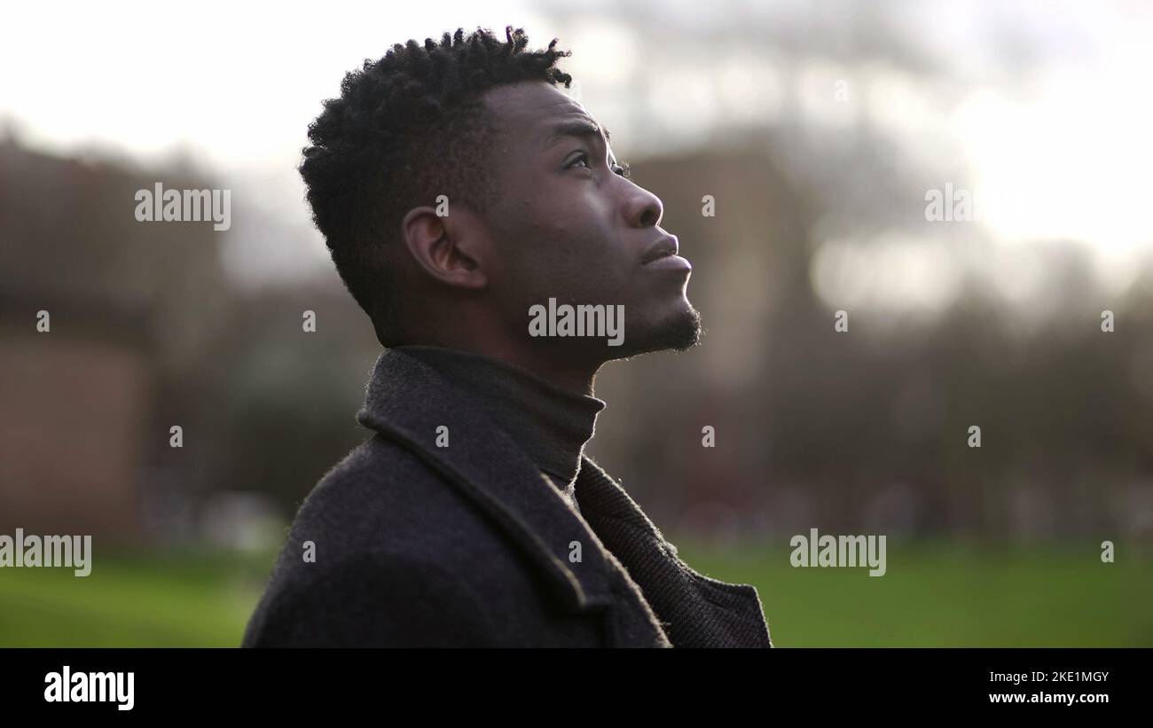 African young black man standing at park looking up in contemplation ...