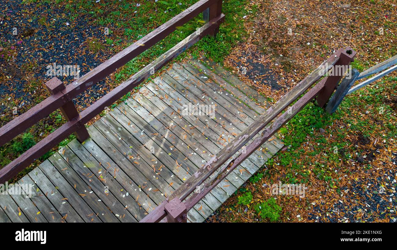 A wooden bridge with fallen leaves in a park during the autumn season ...