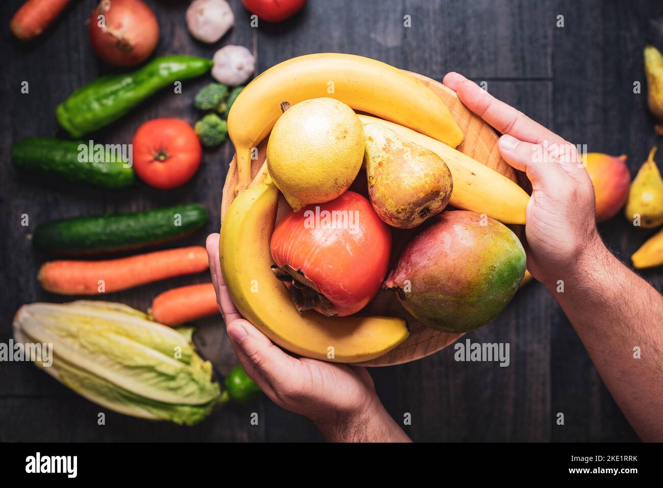 Close-up of hands holding a plate full of fruits on a wooden background ...